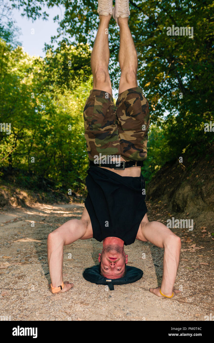 Muscles guy exercising while doing headstand on forest trail Stock ...
