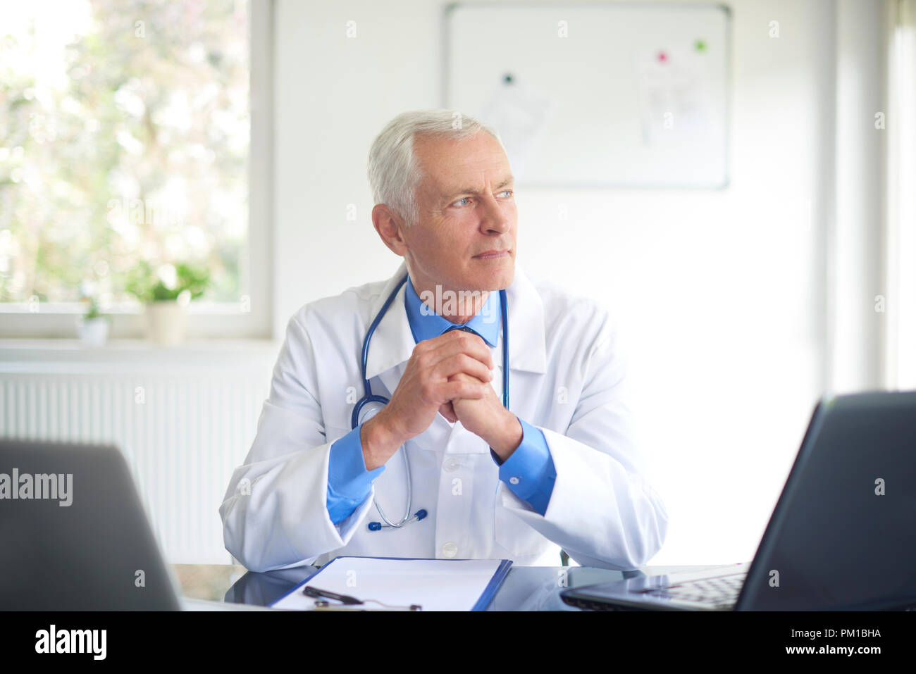 Thinking male doctor sitting in at desk behind computers in the ...
