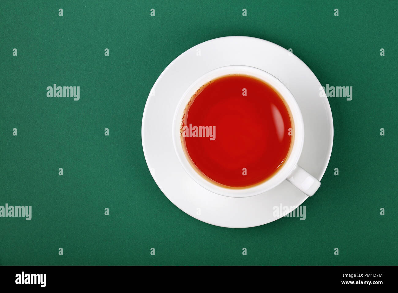 Close up one full white cup of black red tea on saucer on green table ...