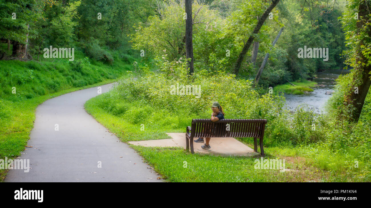Woman sitting on bench between path and lazily flowing river Stock ...