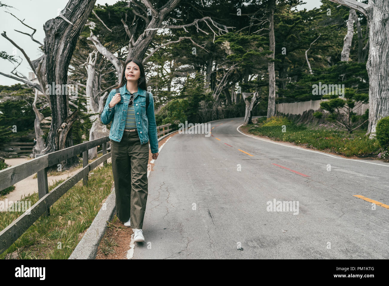 pretty young asian girl walking along the road with trees and plants ...