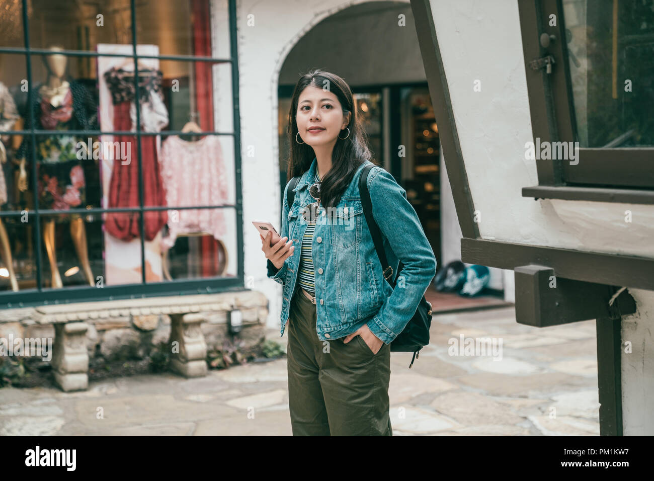 young girl checking her phone and taking a look around the shops ...