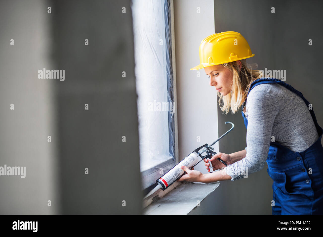 Young woman worker using silicone sealant gun on the construction site ...