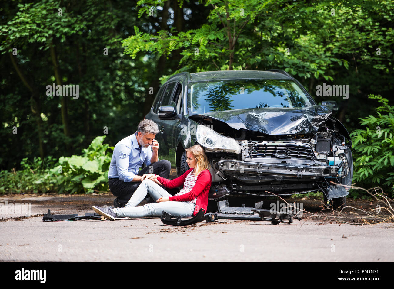 Young woman by the car after an accident and a man making a phone call ...