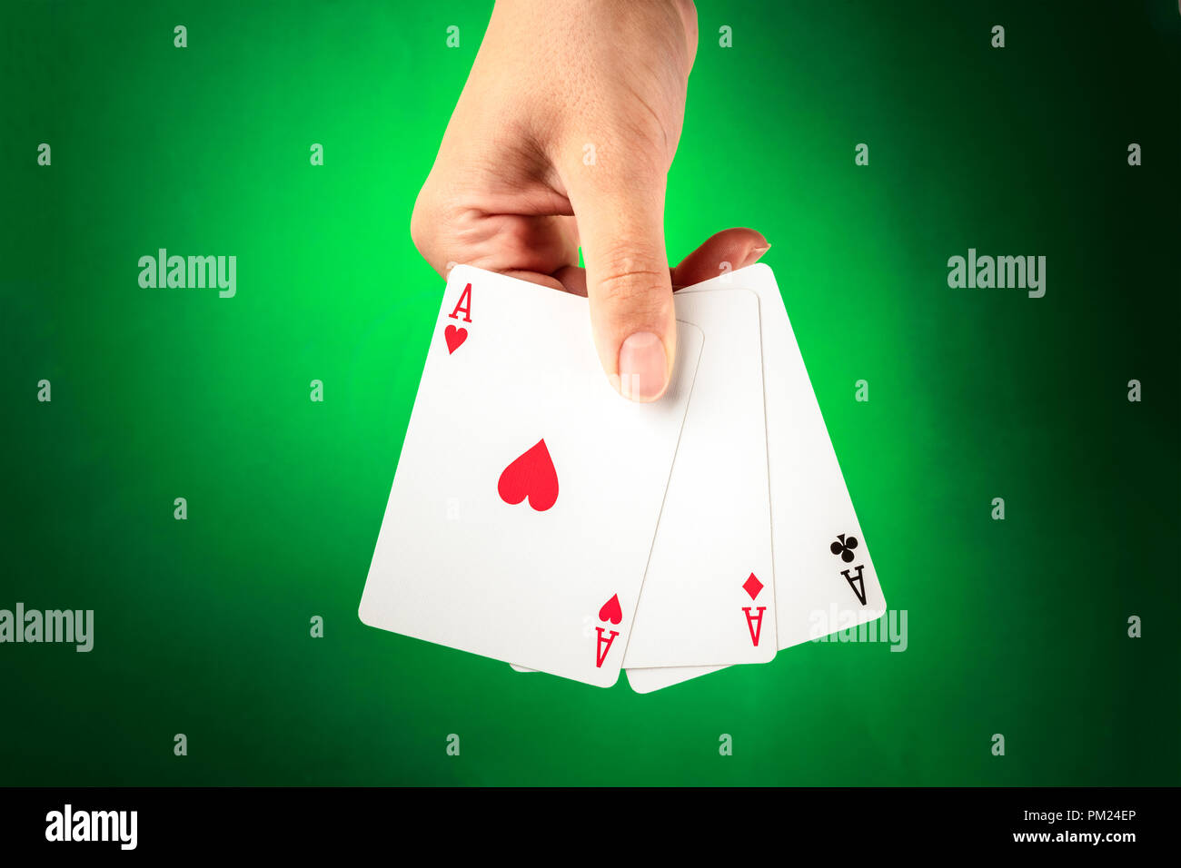 A hand holding three aces against a green background with copy space ...