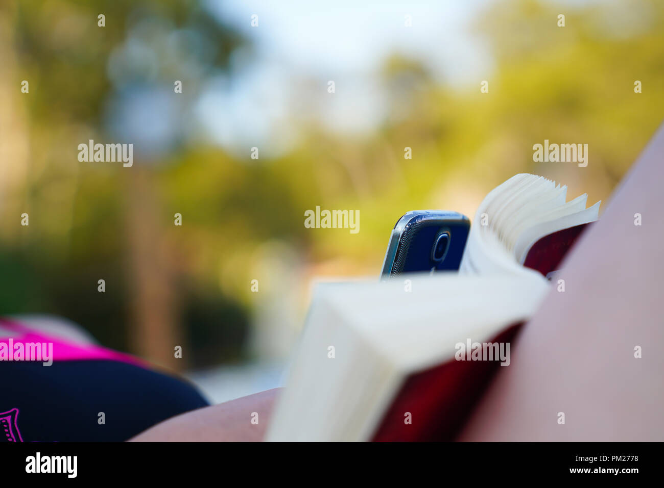 Distracted woman with the mobile phone when reading book and sunbathing ...