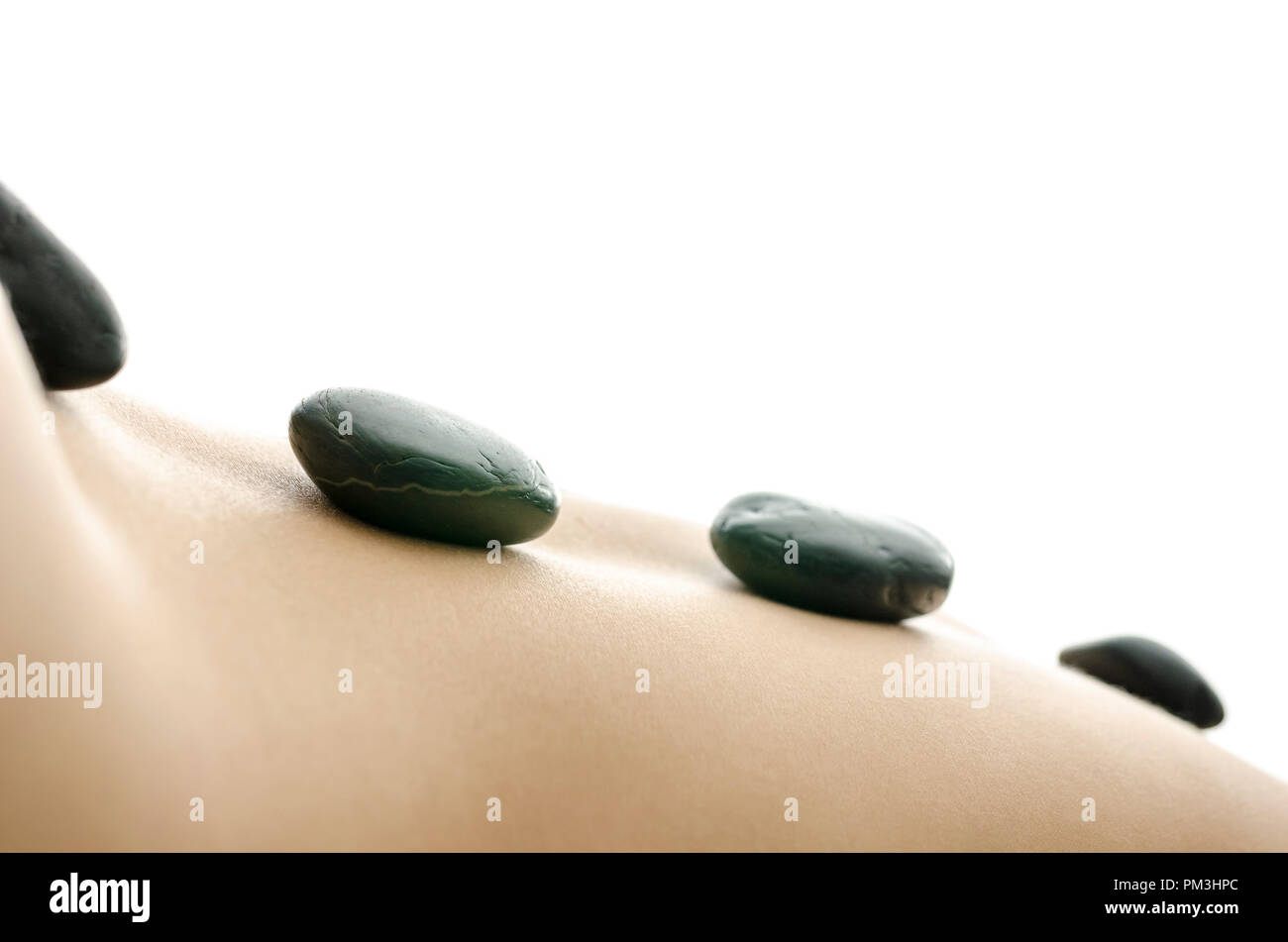 Side view of black massage stones on the back of a woman. With white ...