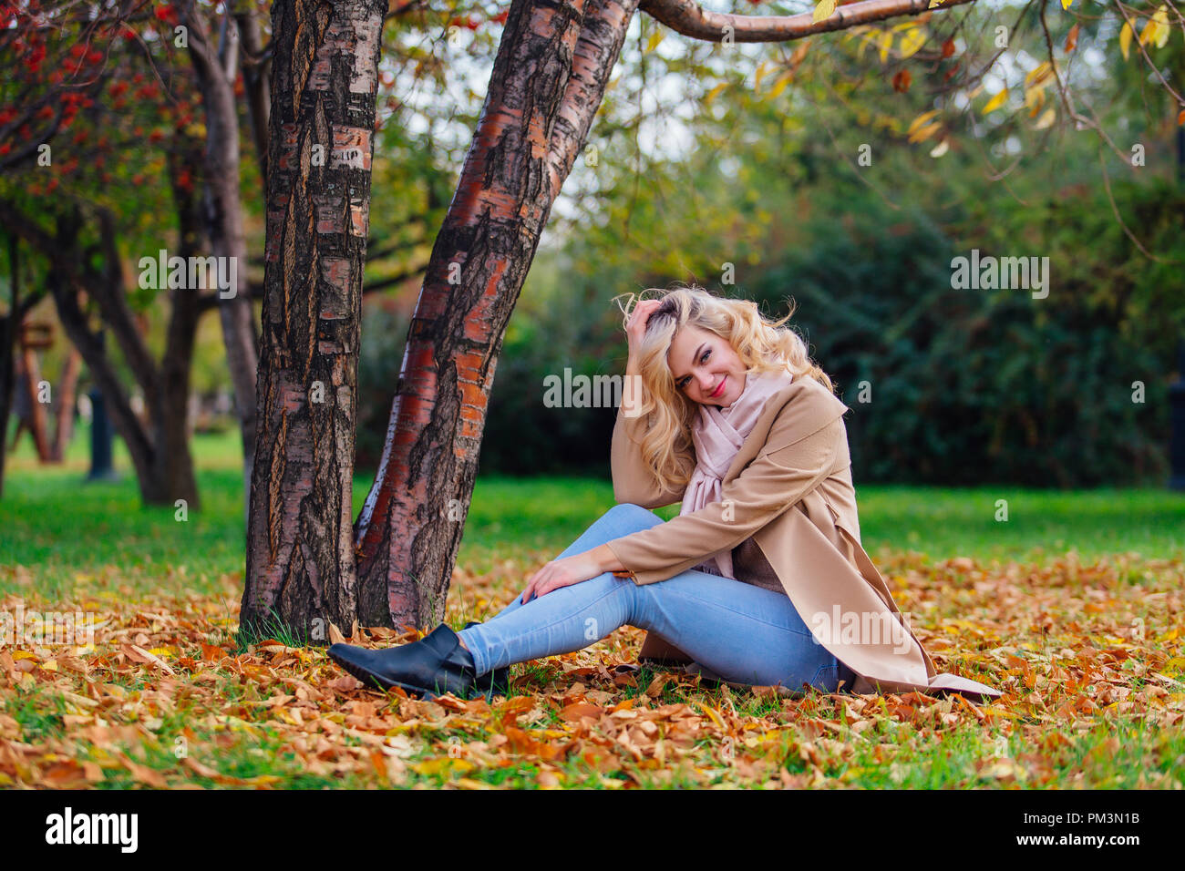 Young beautiful woman sitting under the tree on the ground coverd with ...