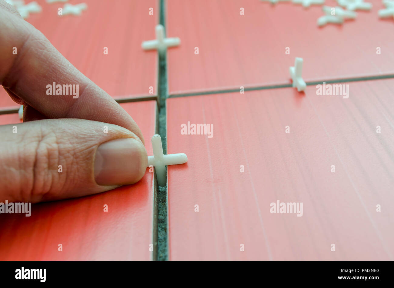 Closeup of tilers hand while using spacer for installing a red ceramic ...