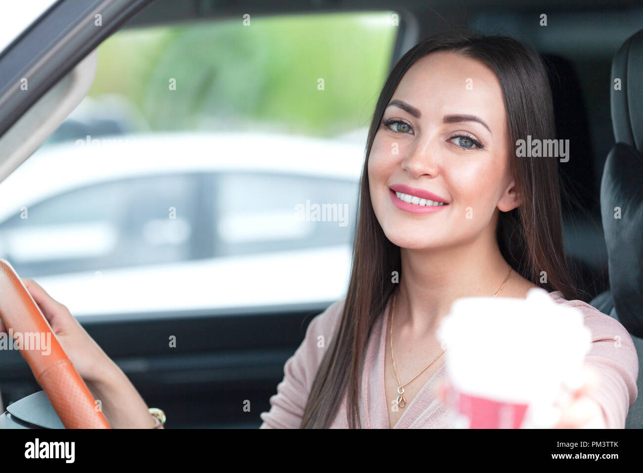 Portrait of pretty smiling friendly girl driver in a car with a paper ...