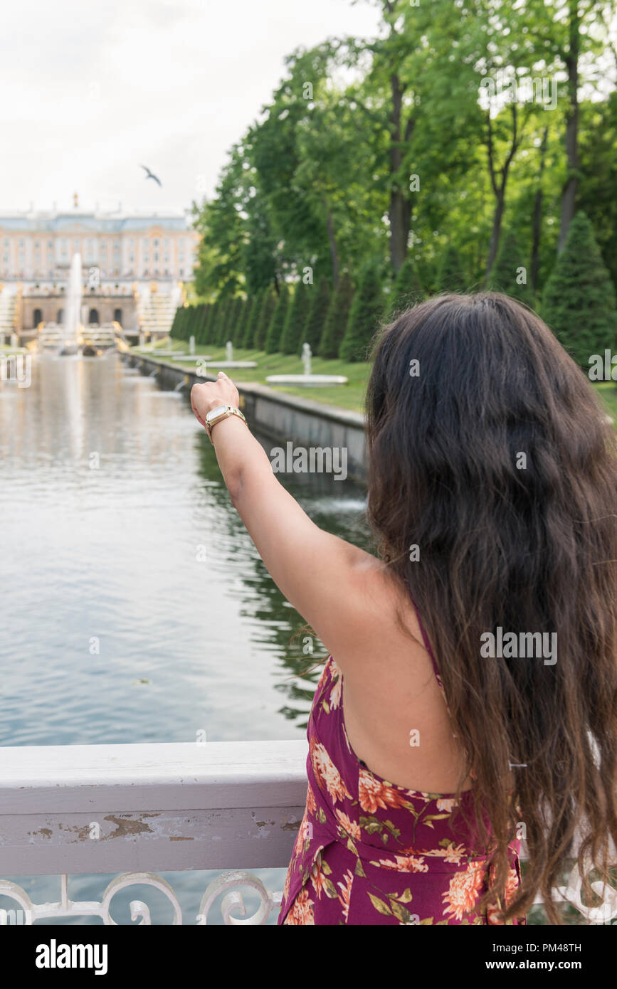 Vertical picture of brunette woman pointing to Peterhof Palace, located ...