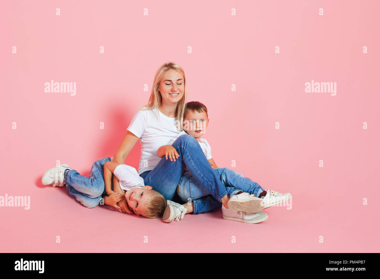 happy mom with two happy sons. Young woman and two baby boys, pink ...