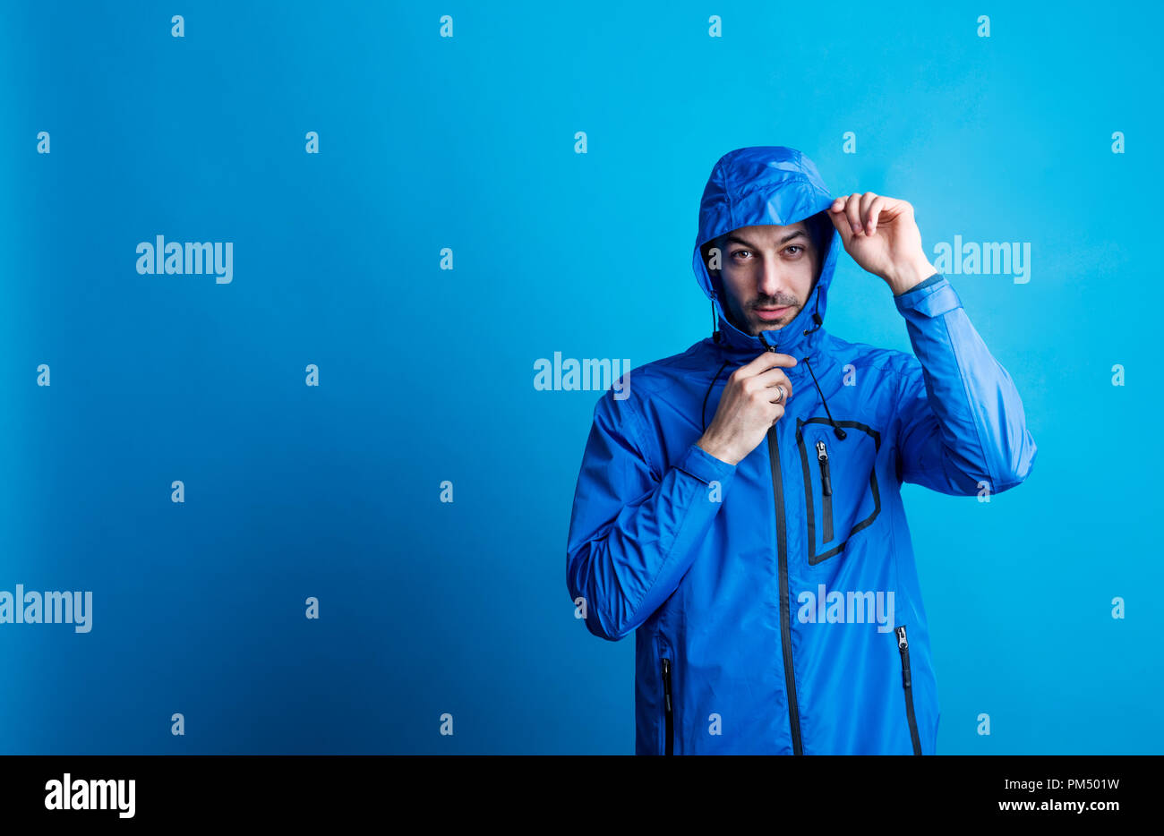 Portrait of a young man in a studio with anorak on a blue background ...