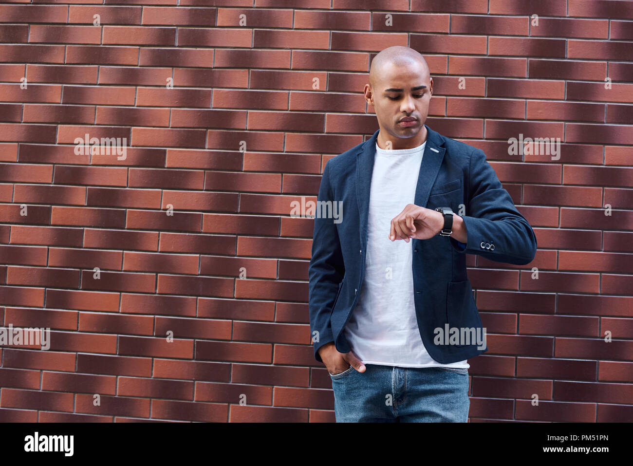 Time management. Young guy standing on wall looking at watch concerned ...