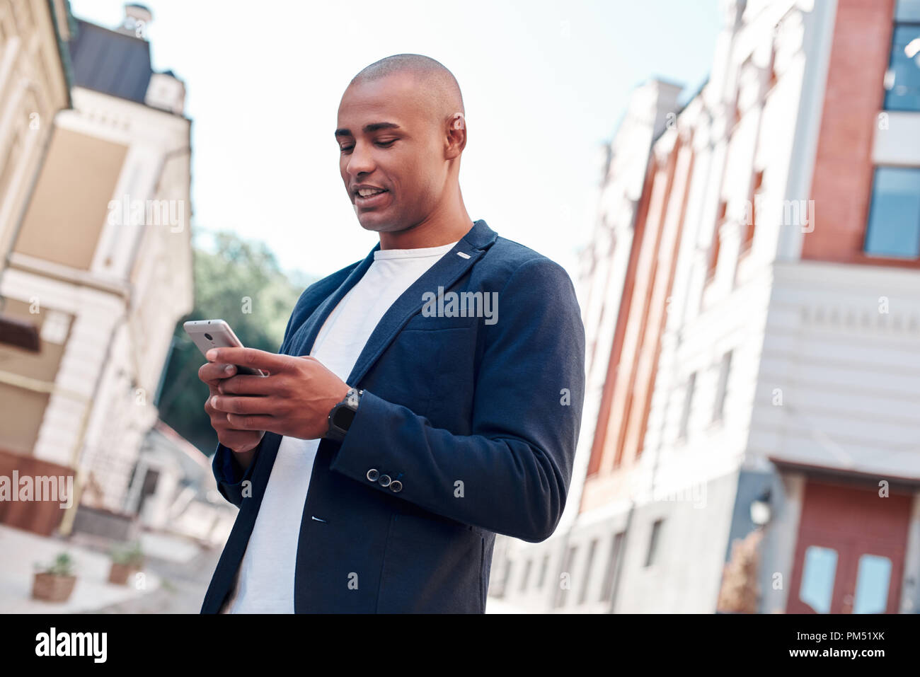 Using gadget. Young man walking on the city street using application on ...