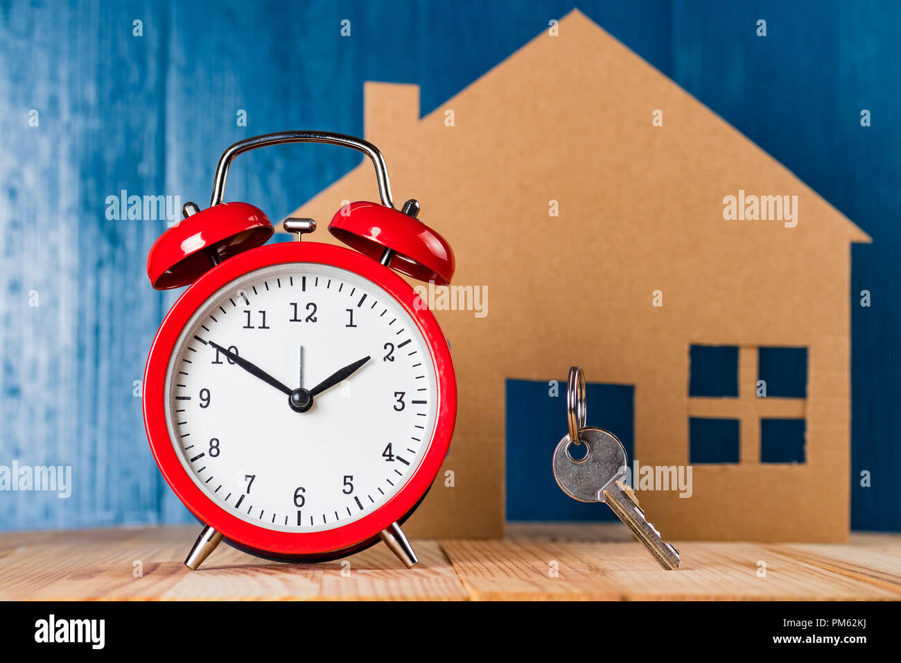 Old vintage alarm clock and door key against house shape and blue ...