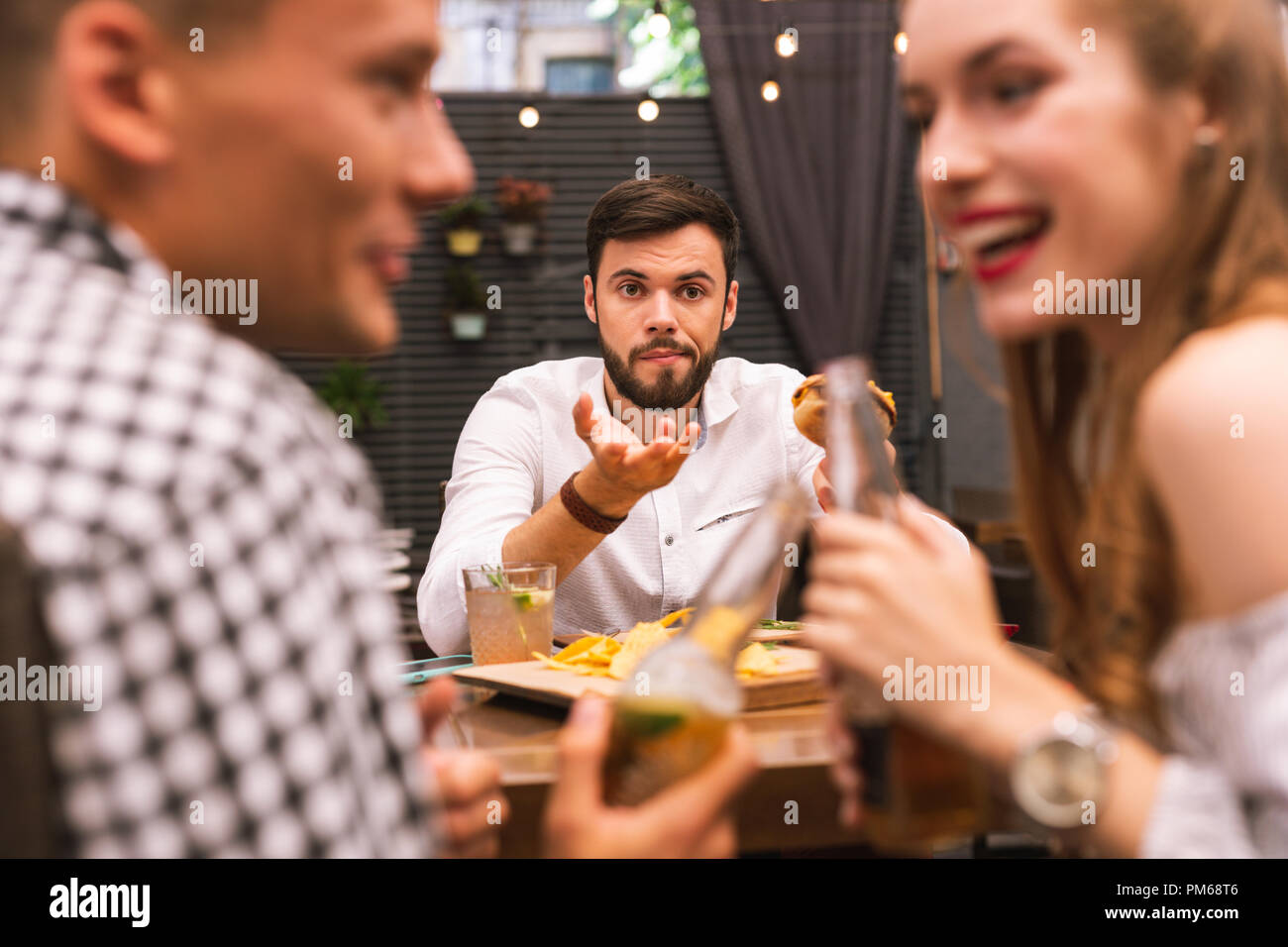 Offended young man looking at his friends while eating burgers Stock ...