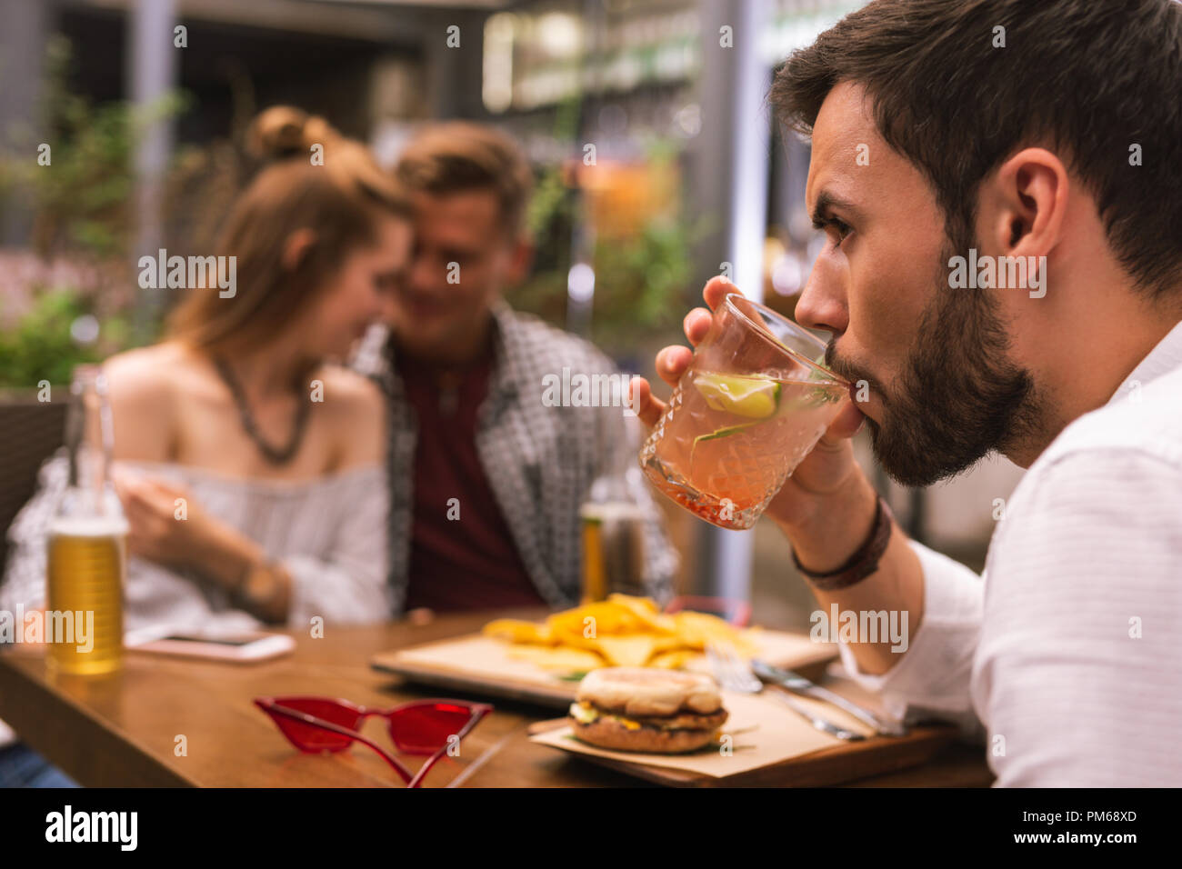 Young man enjoying cold drink while his friends hugging Stock Photo - Alamy