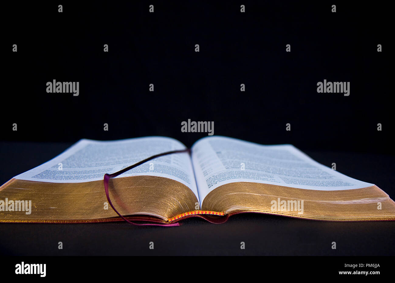 Bible opened up with worn gold on pages isolated on black background ...