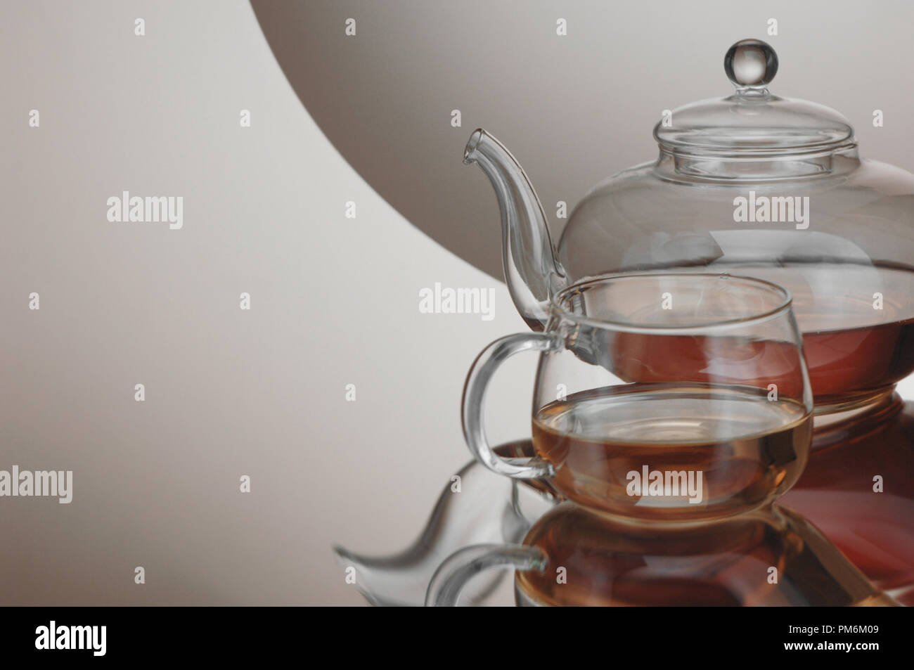 transparent teapot with teacup on the reflective surface on a light ...