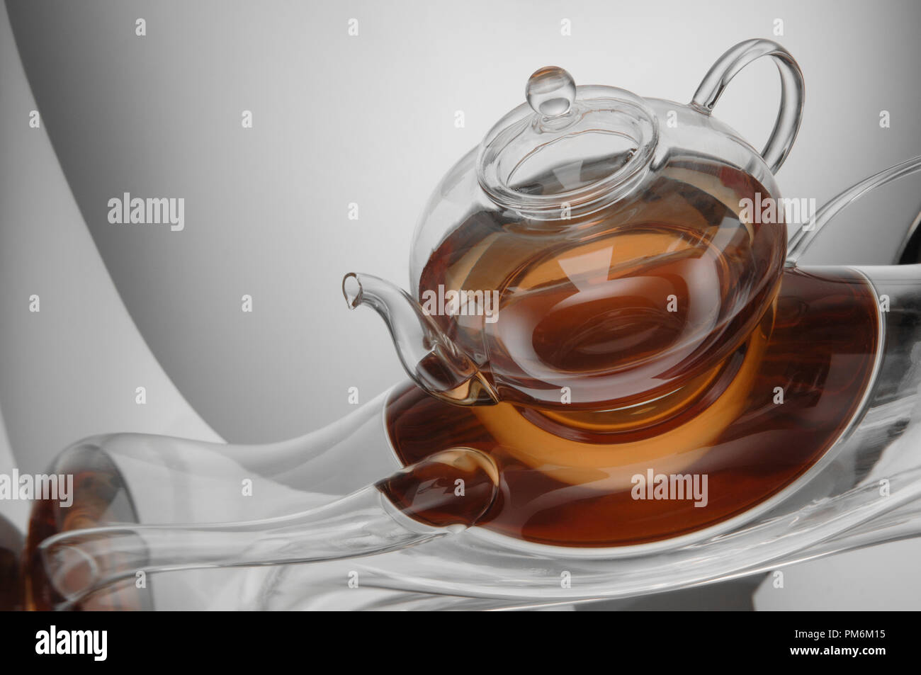 transparent teapot with tea on the reflective surface on a light gray ...