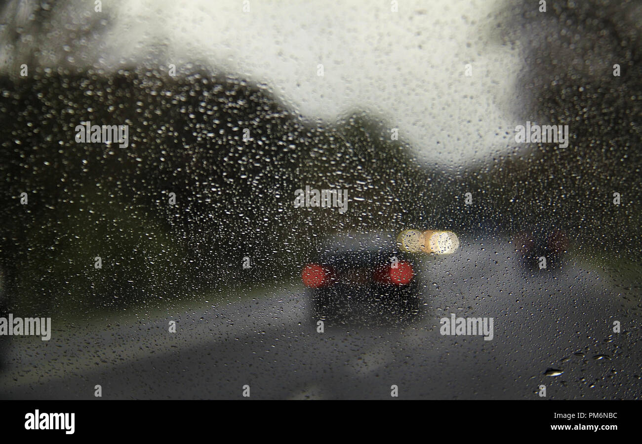Cars with headlights on viewed through a raindrop-covered windshield ...