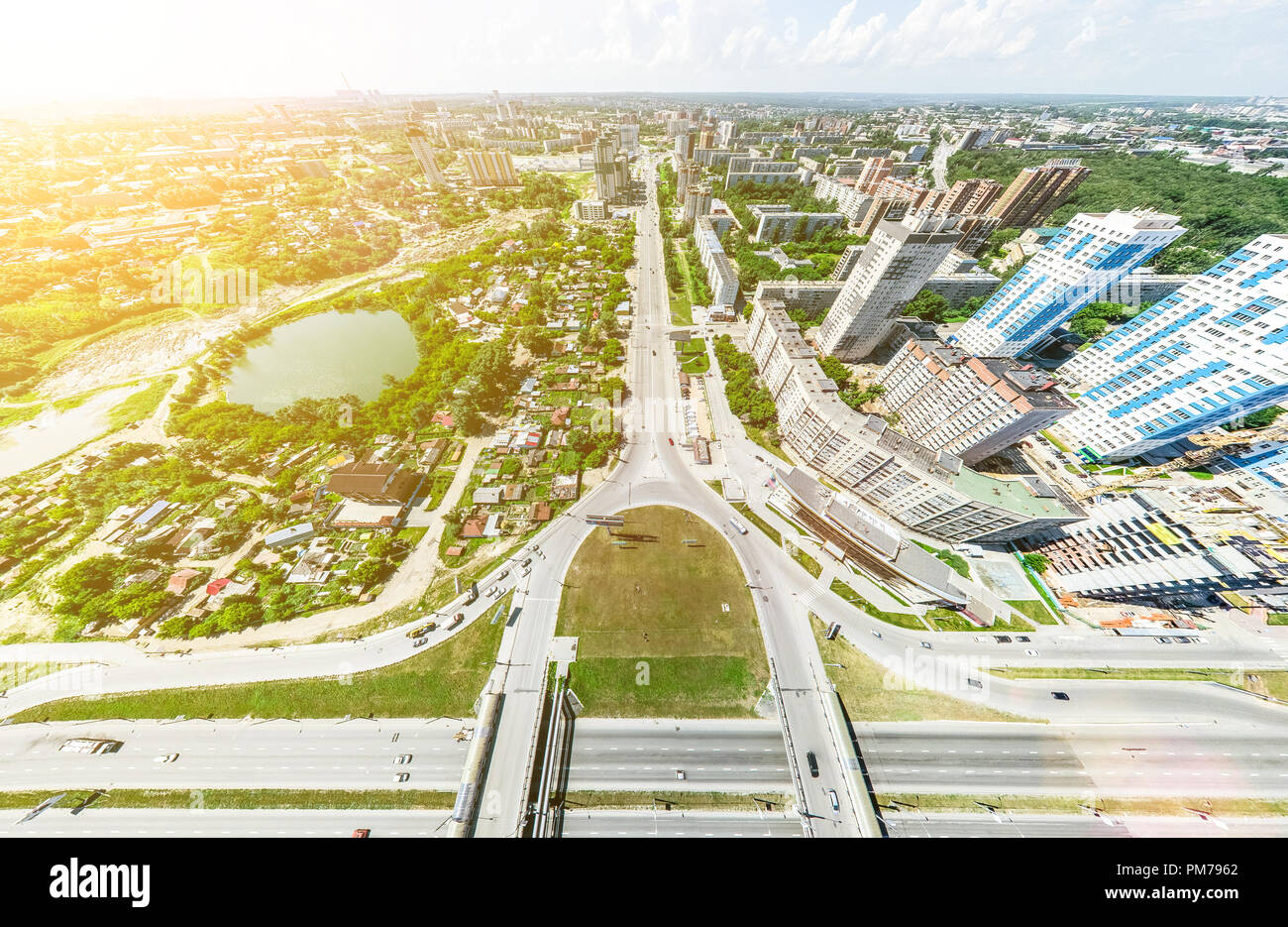 Aerial city view with crossroads and roads, houses, buildings, parks and parking lots. Sunny ...