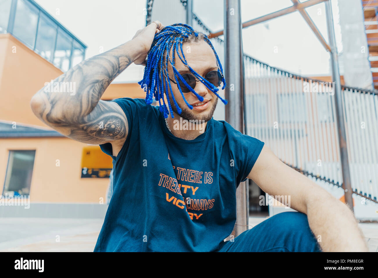 Young attractive man with blue dreadlocks touching his hair, and ...