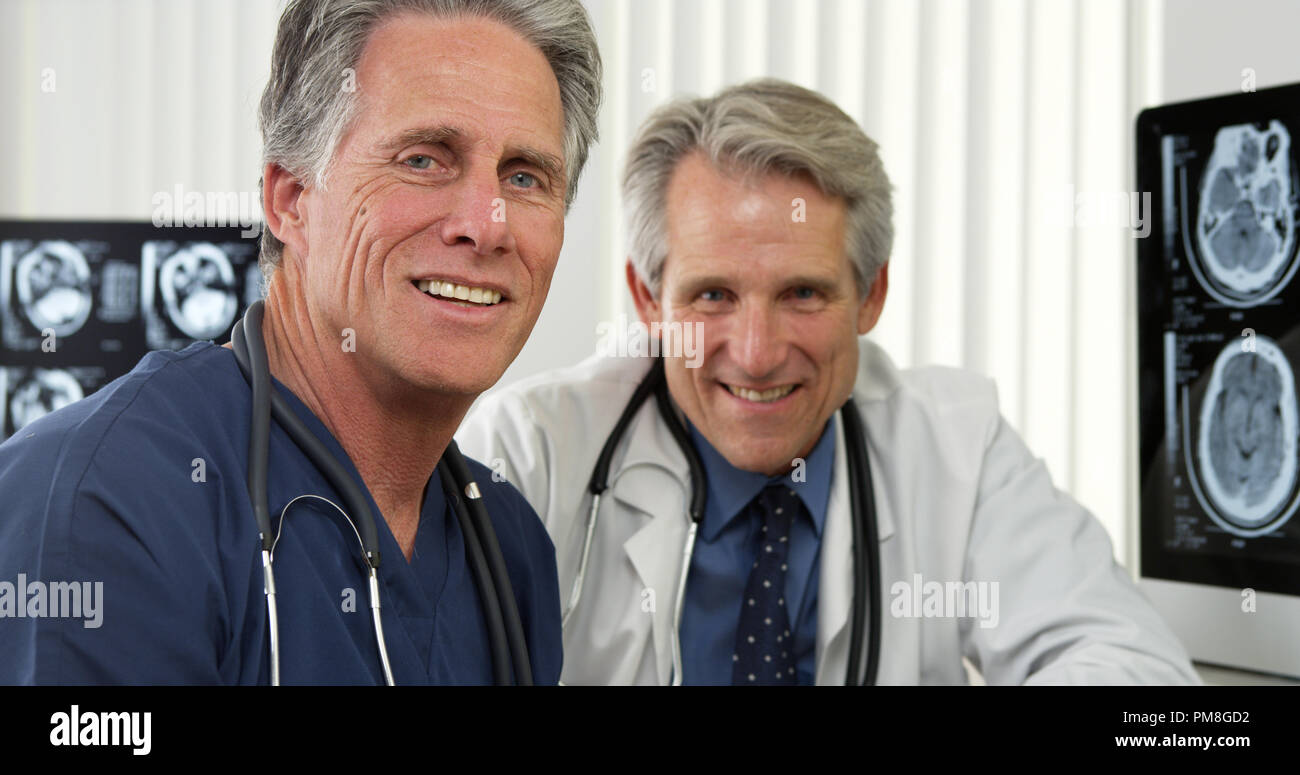 Senior doctors sitting at desk smiling Stock Photo - Alamy