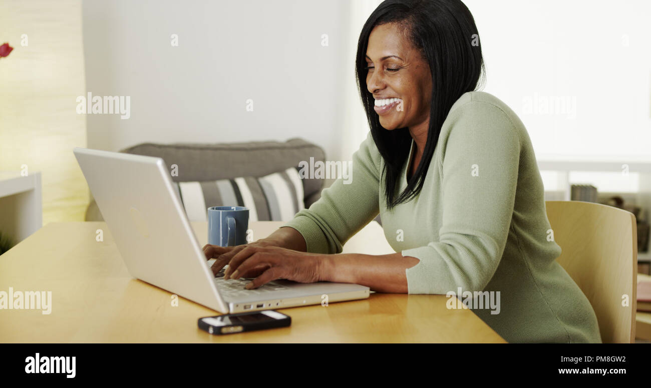Healthy African American woman laughing and typing on her laptop Stock ...