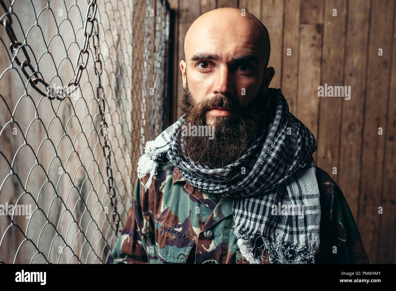 Bearded terrorist in uniform in front of metal grid, male mojahed ...