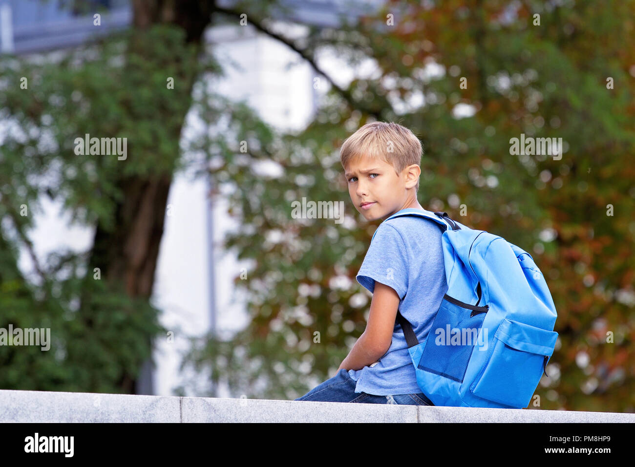 Boy sitting near school, back view, he turns around and look on camera ...