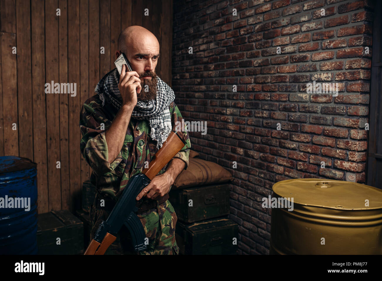 Terrorist in uniform holds kalashnikov rifle and mobile phone in hands ...