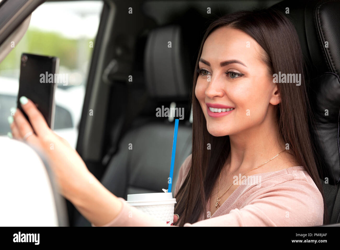 Portrait of pretty smiling friendly girl driver doing a selfie in a car ...