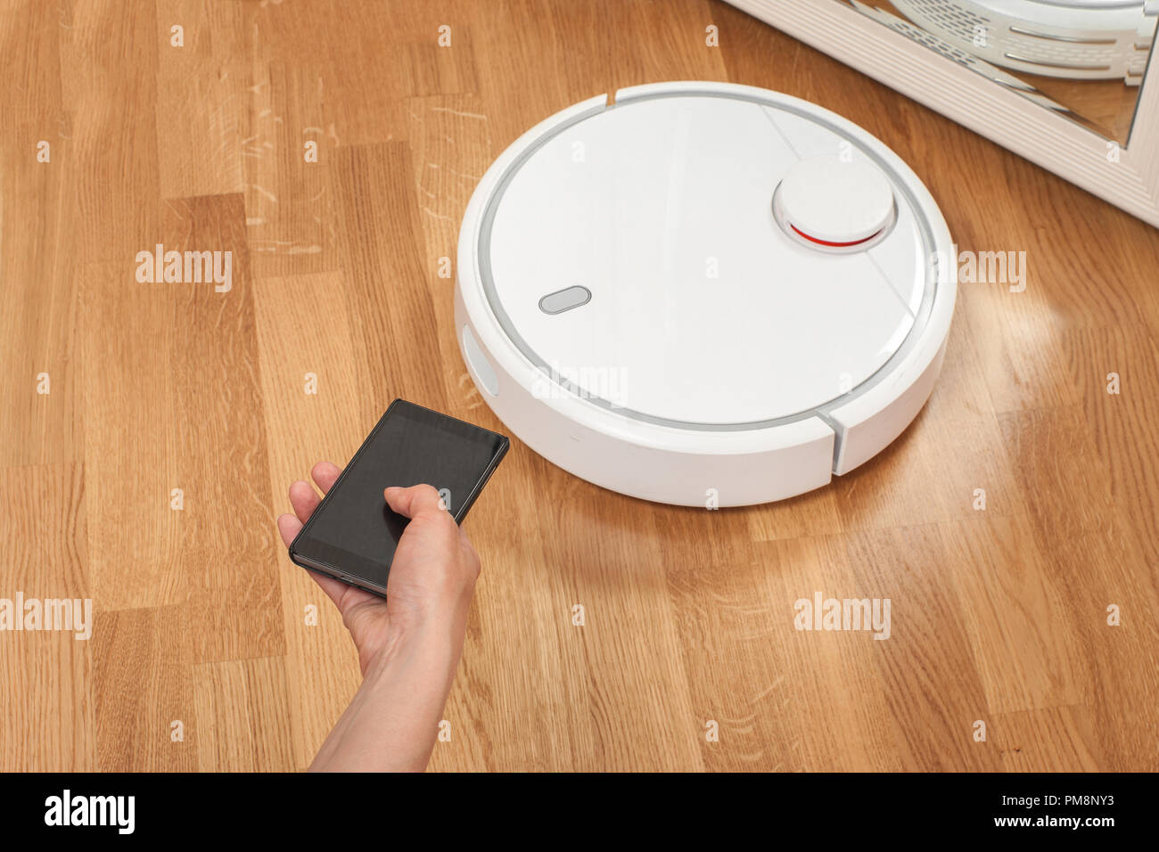 womens hand using mobile to control white robotic vacuum cleaner ...