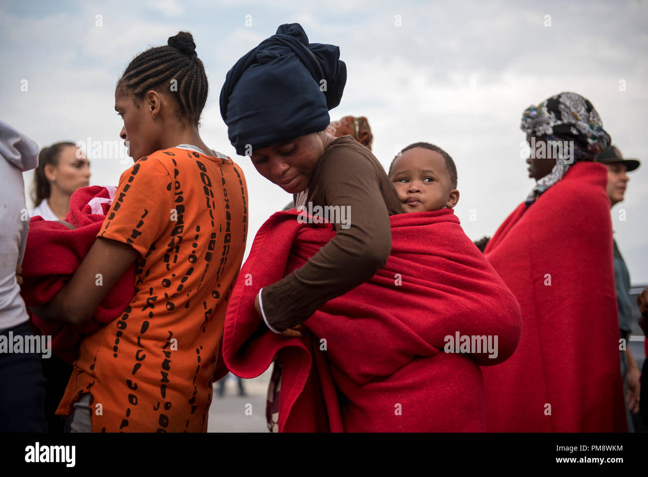 Sub Saharan woman seen holding her baby with a red blanket after being ...