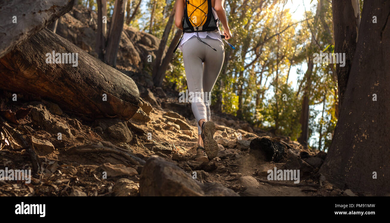 Rear view of fit woman with hydration pack running over a rocky trail ...