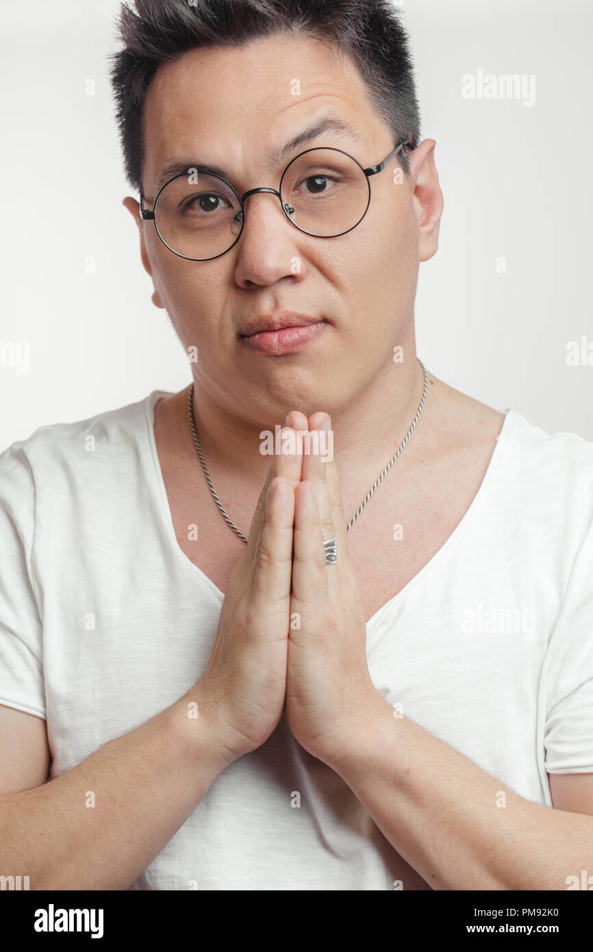 Asian man in t-shirt, holding hands in pray, begging for help or asking ...