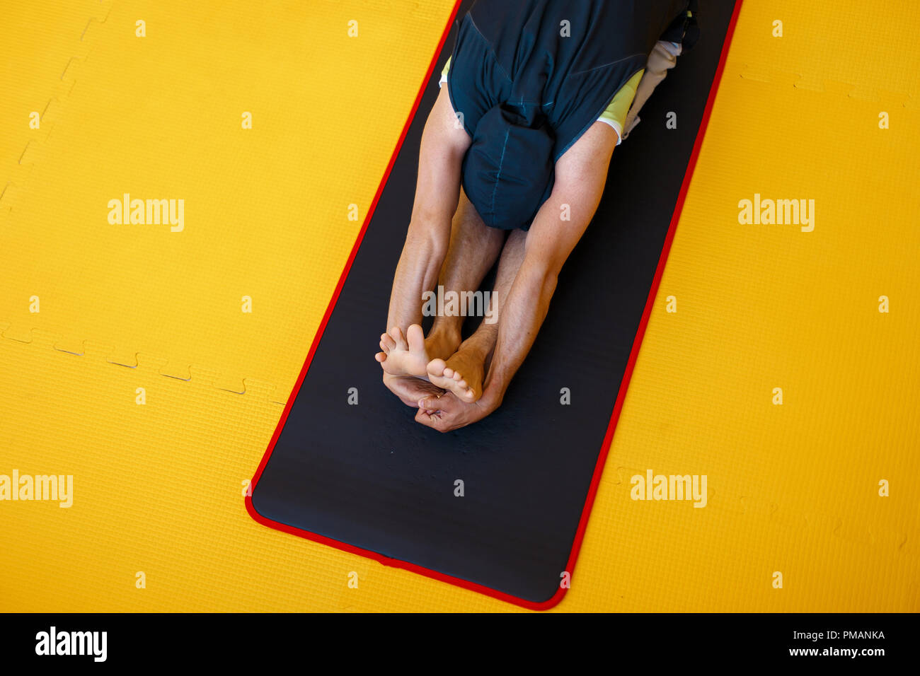 Athletic man in hood in sportswear doing stretching on yellow ...