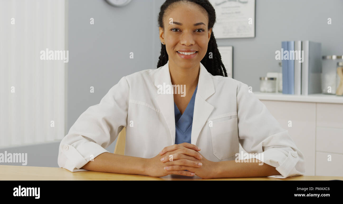 Black woman doctor sitting at desk smiling Stock Photo - Alamy