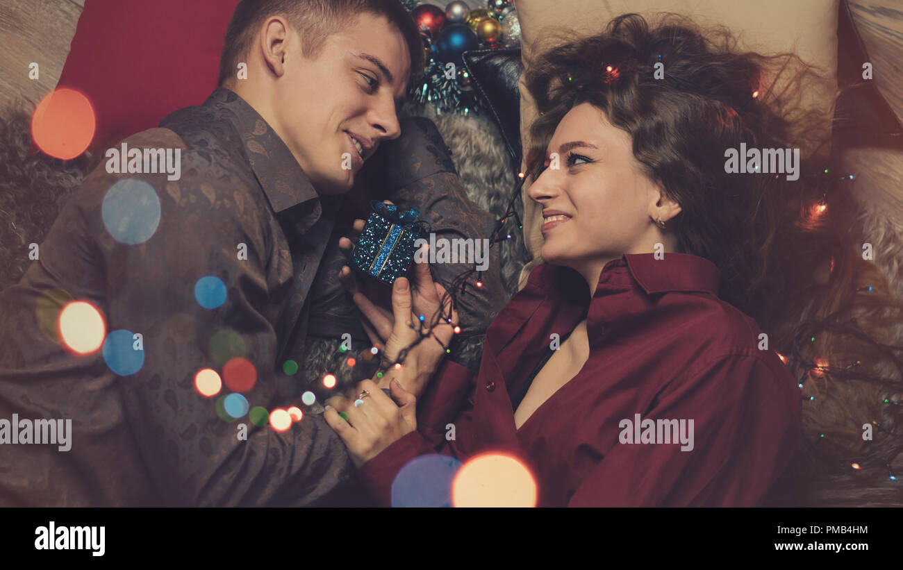 Loving couple celebrating Christmas. They lie on couch and look into ...