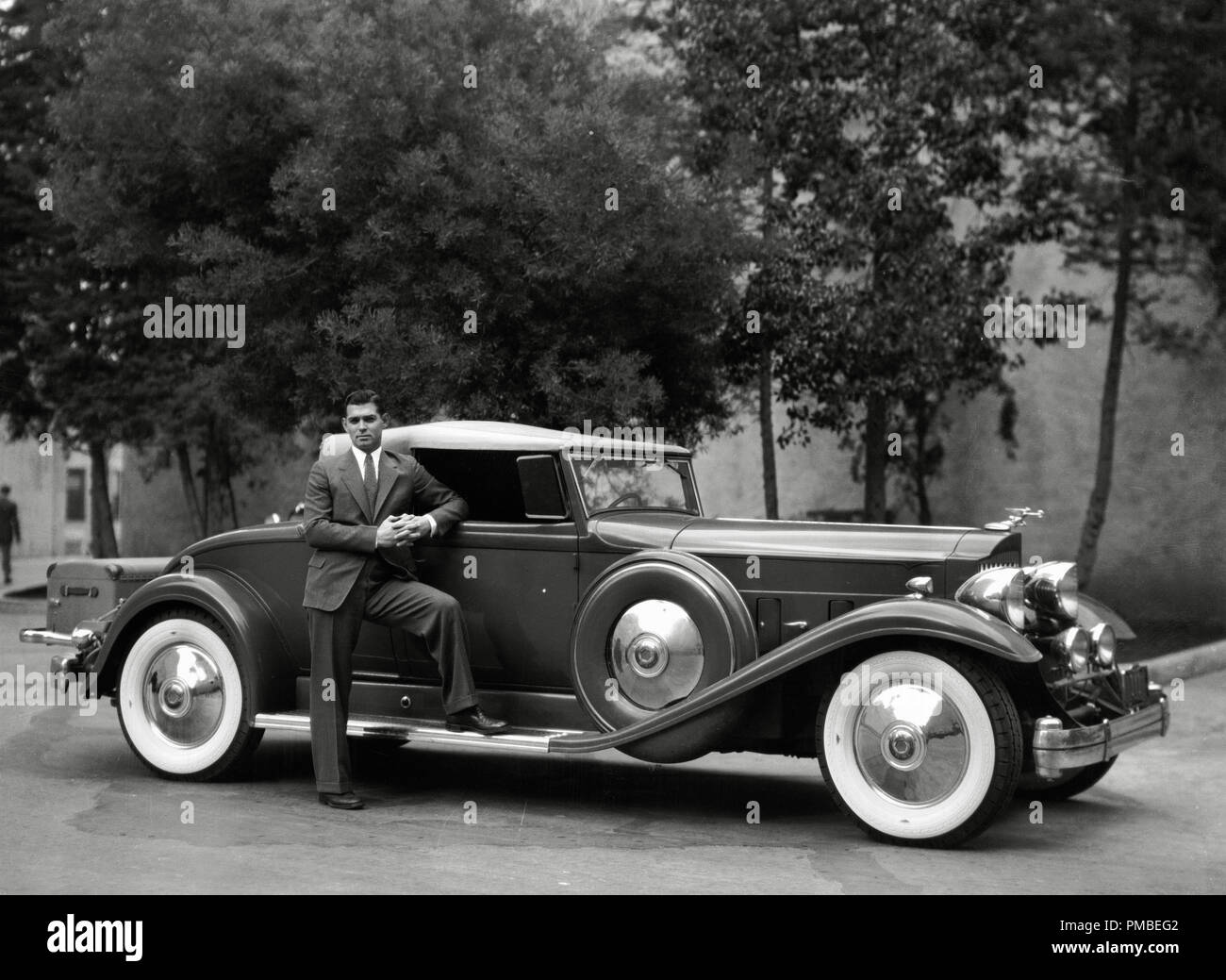 Clark Gable, wearing a suit, poses next to his luxury automobile, circa ...