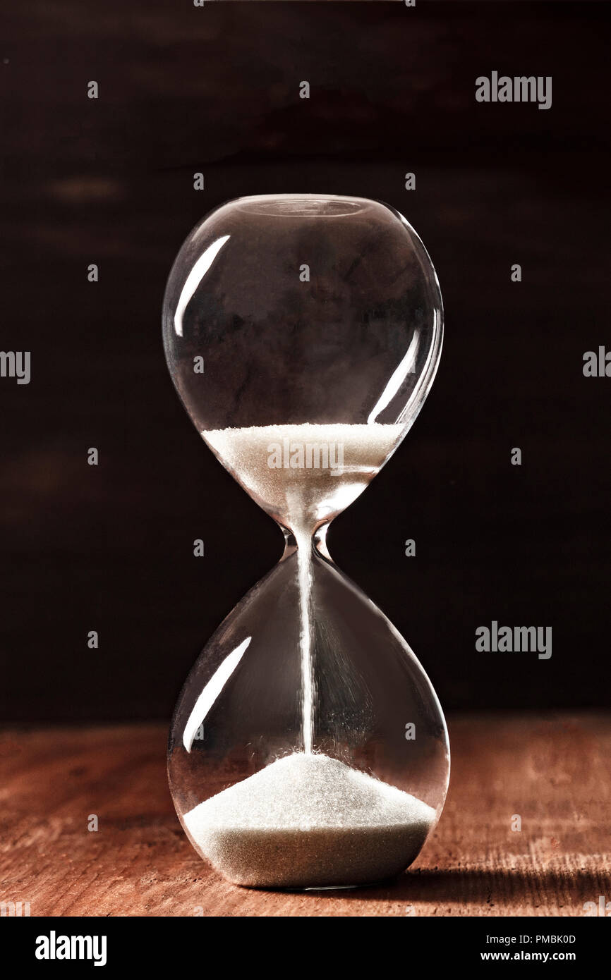 A side view of an hourglass with falling sand, on a dark background ...