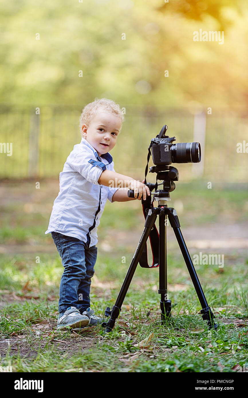 Two years old boy is photographer. Kid holds a camera on tripod and ...