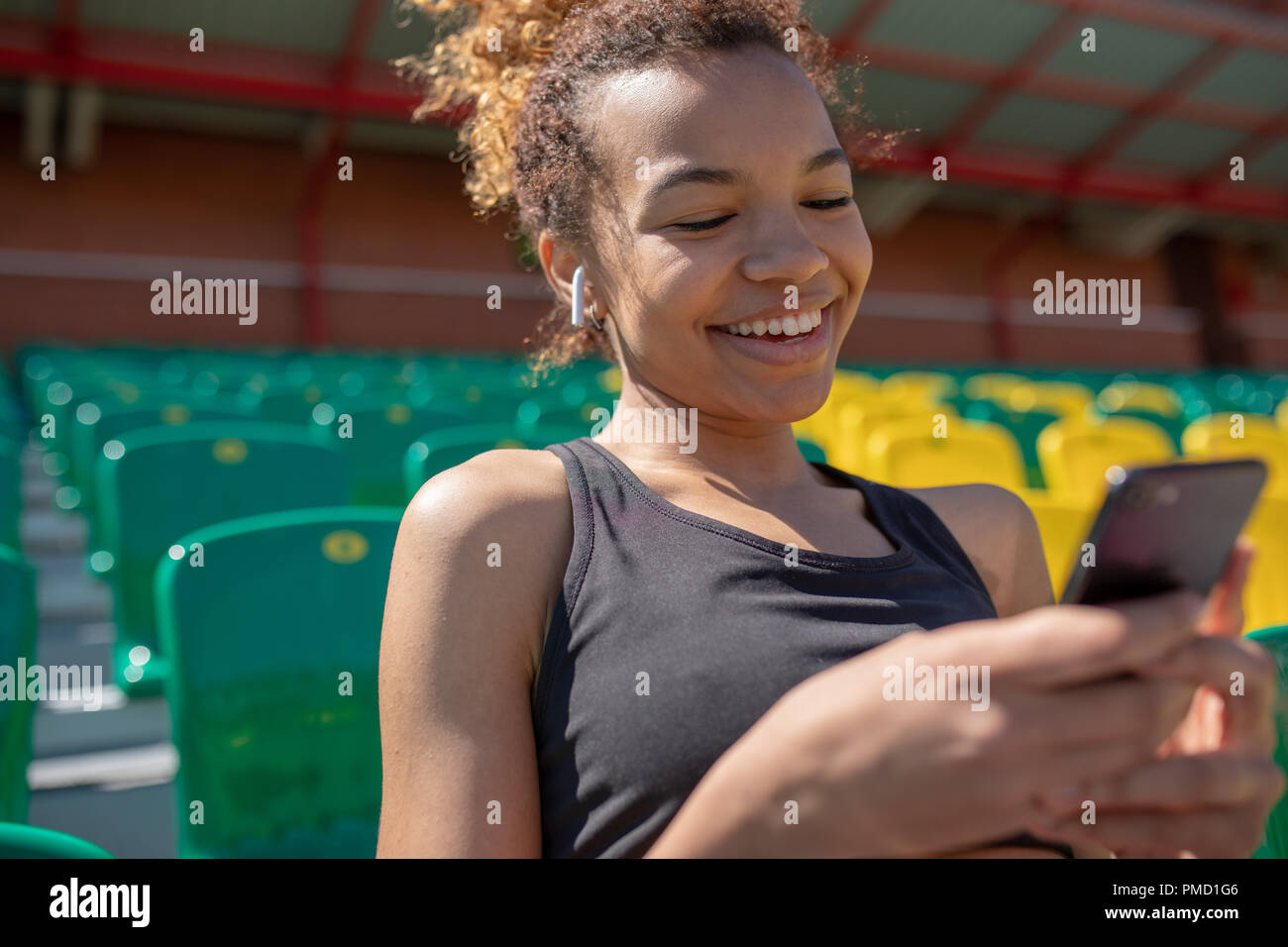 Young woman sitting on the stadium tribune after training and using ...