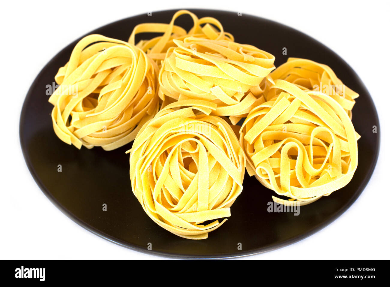 Uncooked tagliatelle on black ceramic plate. Isolated Stock Photo - Alamy