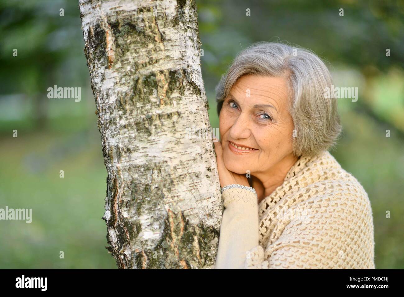 Nice happy old woman standing by the tree Stock Photo - Alamy