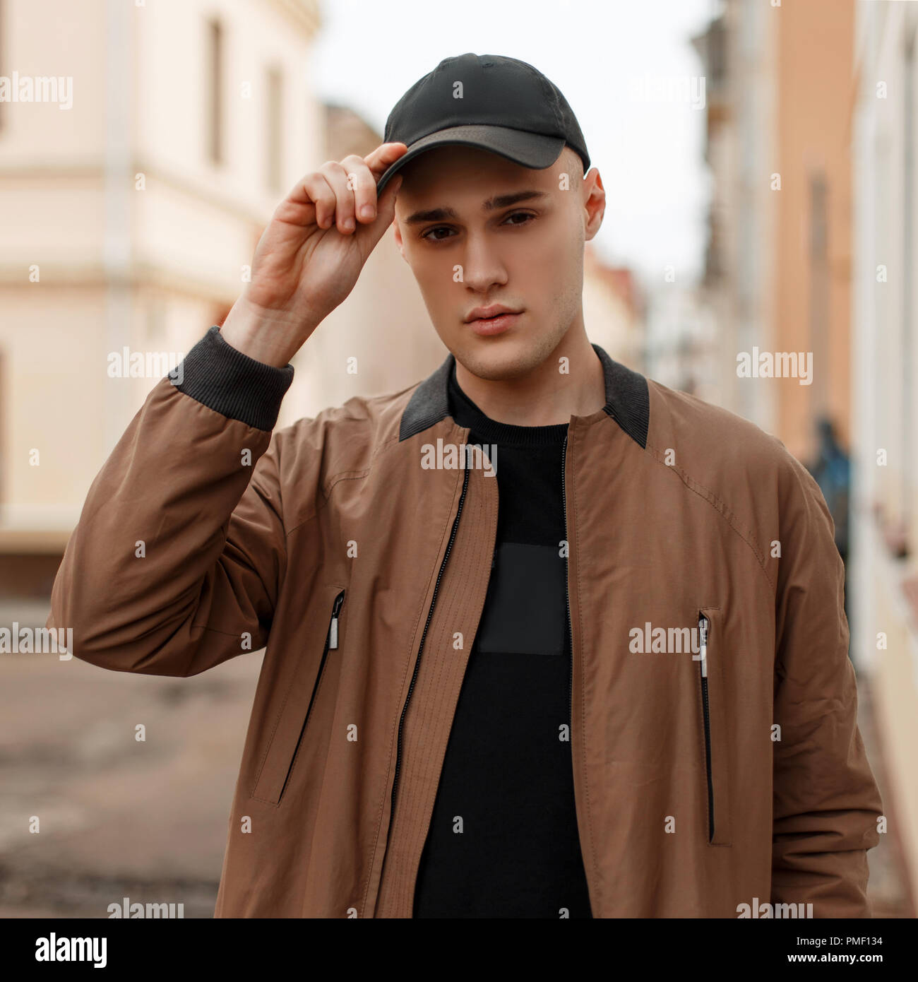 handsome stylish guy with a vintage coat with a black cap and bag walks ...