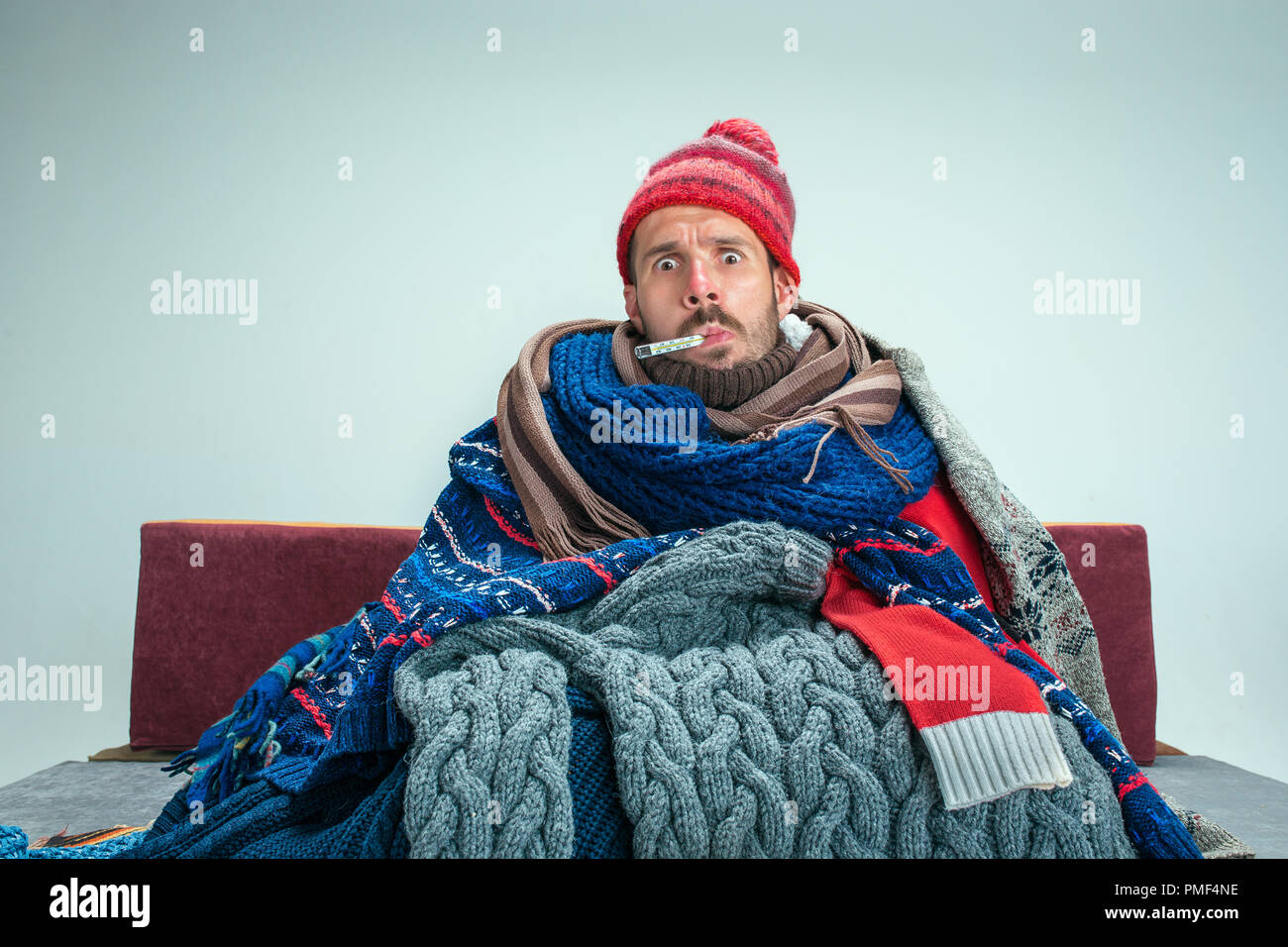 Bearded sick man with flue sitting on sofa at home or studio with ...