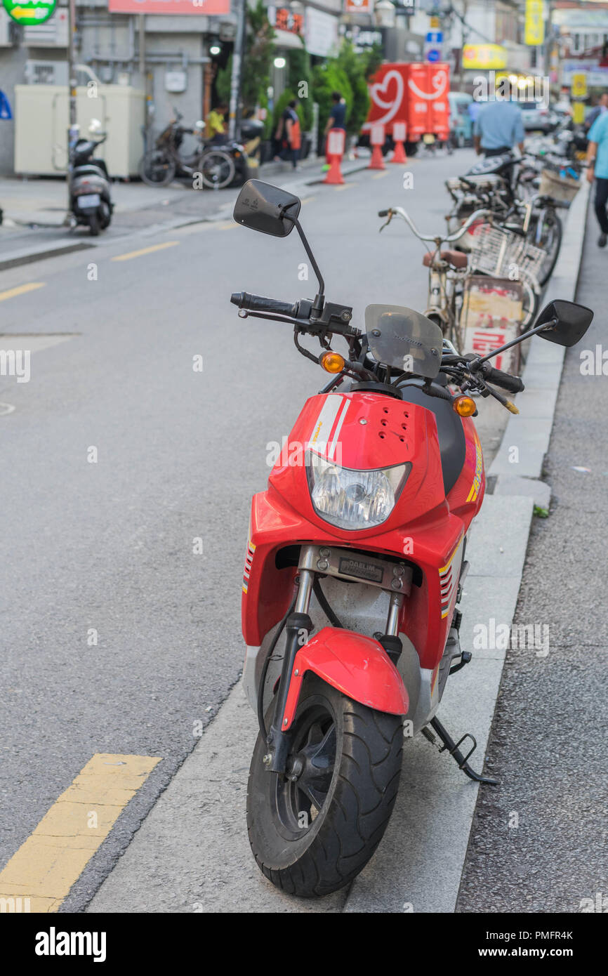 A city street with a long line of parked scooters and bicycles, in ...